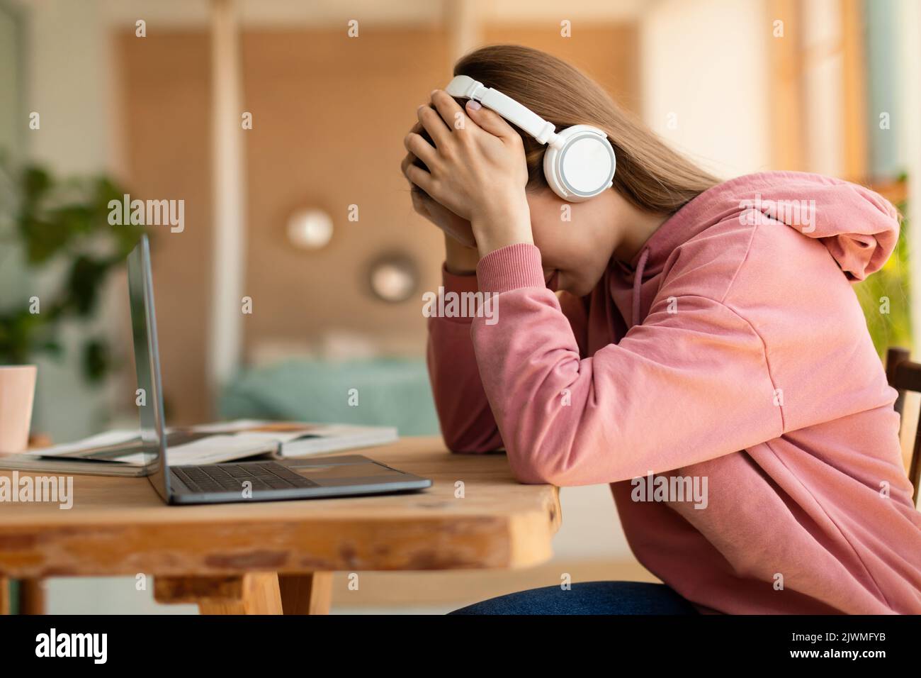 Tired upset teen girl holding head with hands while studying online on ...