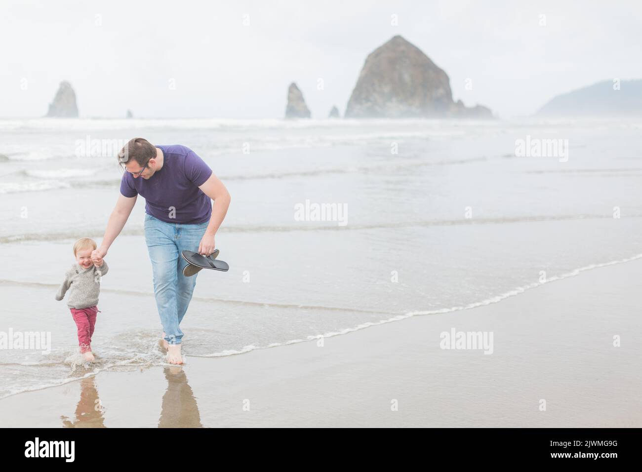 Father and toddler son walk in water in Cannon Beach, laughing Stock ...