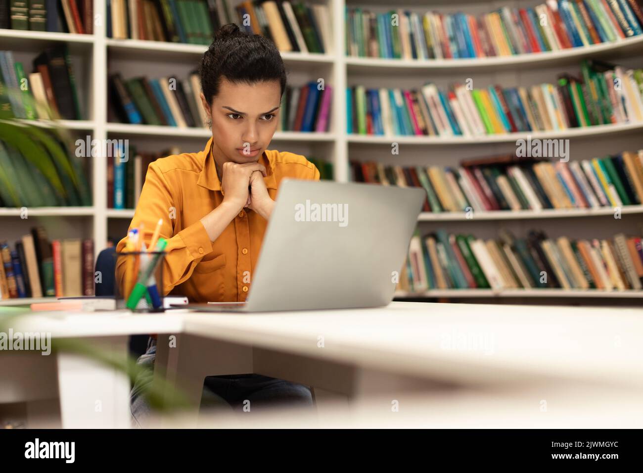 Serious mixed race lady sitting at desk using laptop, looking at pc ...