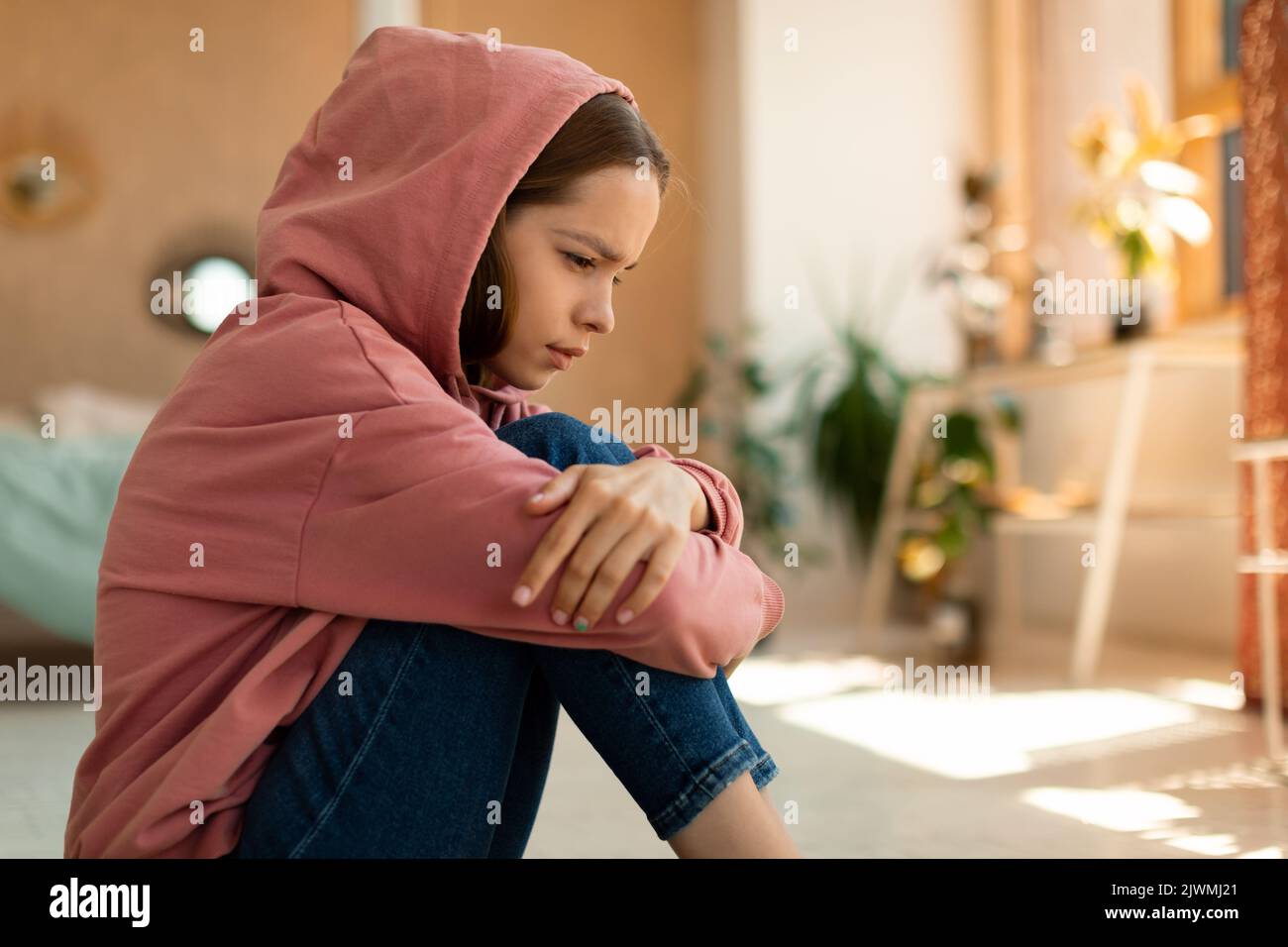 Upset teenager girl wearing hood, hugging her knees, having ...