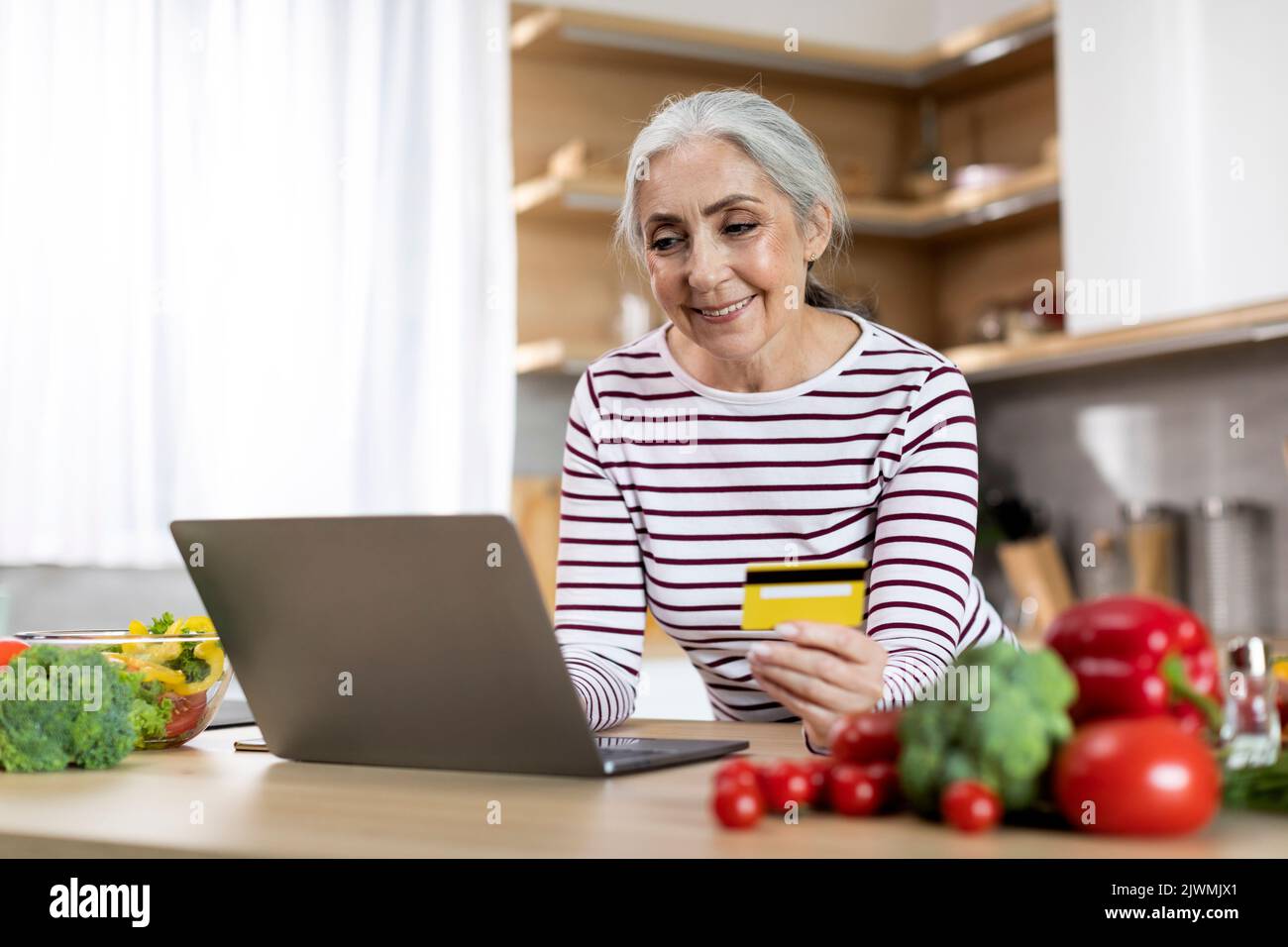 Elderly Lady Using Laptop And Credit Card In Kitchen, Ordering ...