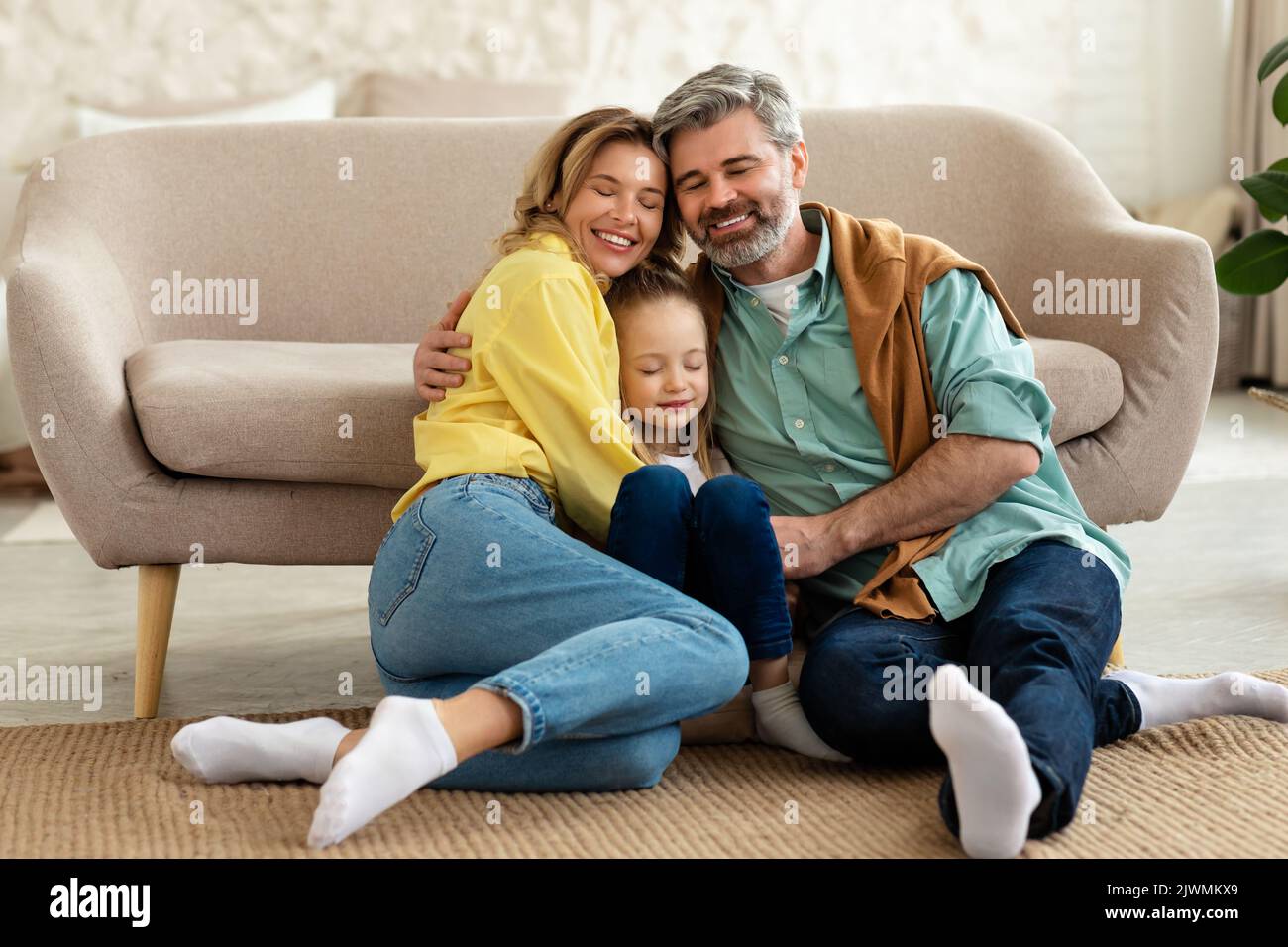 Parents Hugging Little Daughter Posing With Eyes Closed At Home Stock Photo - Alamy