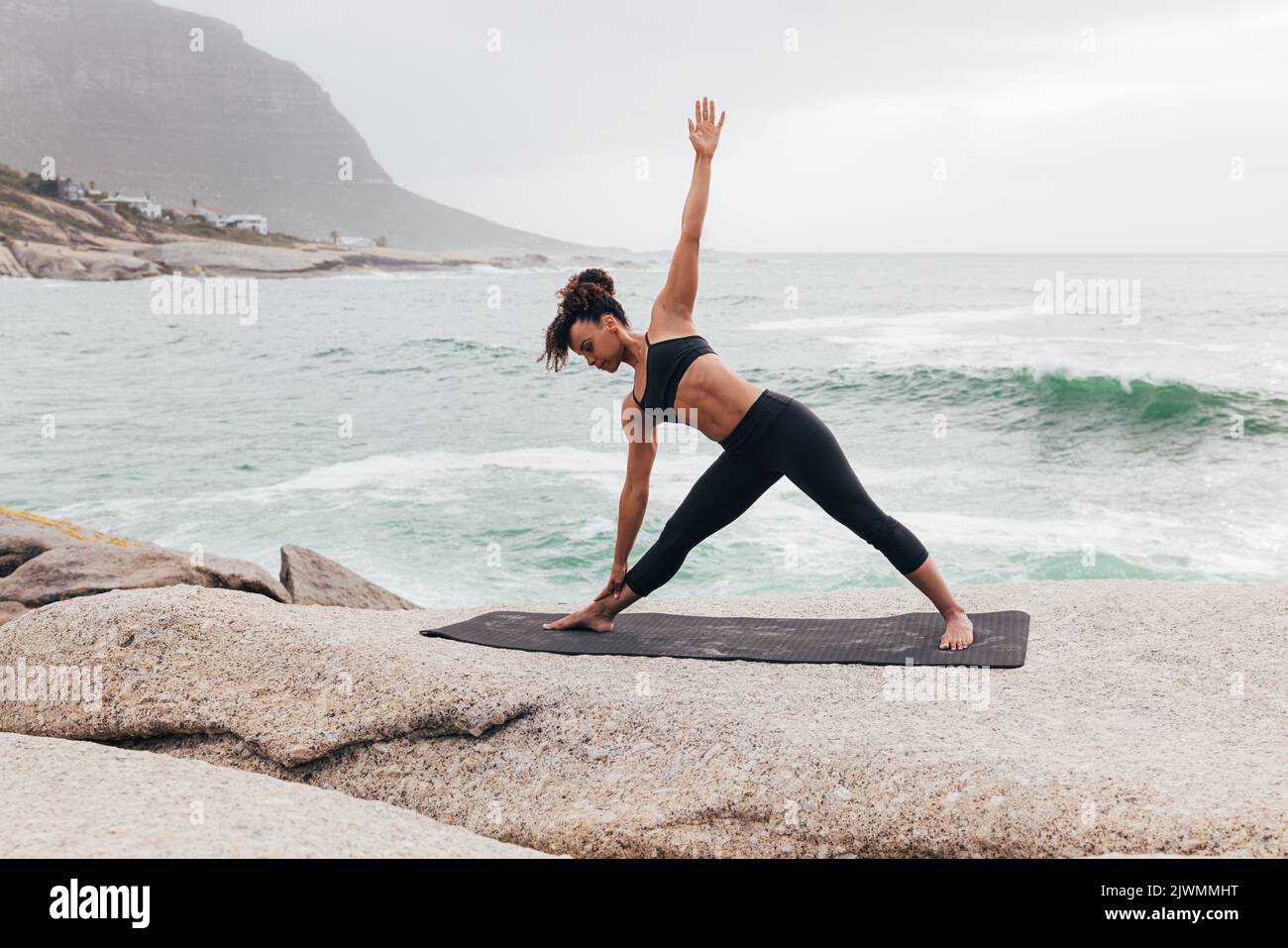 Woman practicing Utthita Trikonasana pose by ocean at sunset. Full ...