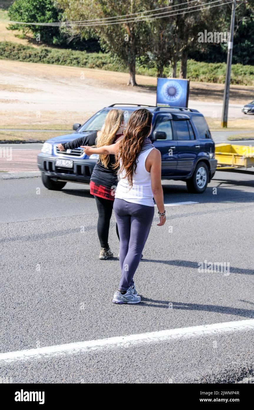 Two young girl tourists hitch-hiking on a busy main road in Taupo near ...