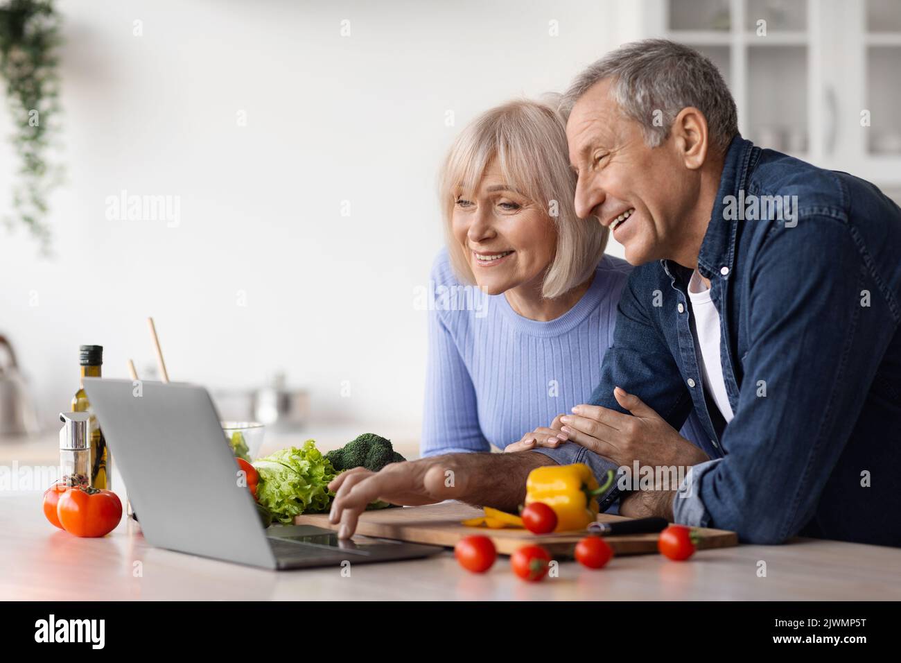 Cheerful senior couple watching food vlog while cooking, copy space ...