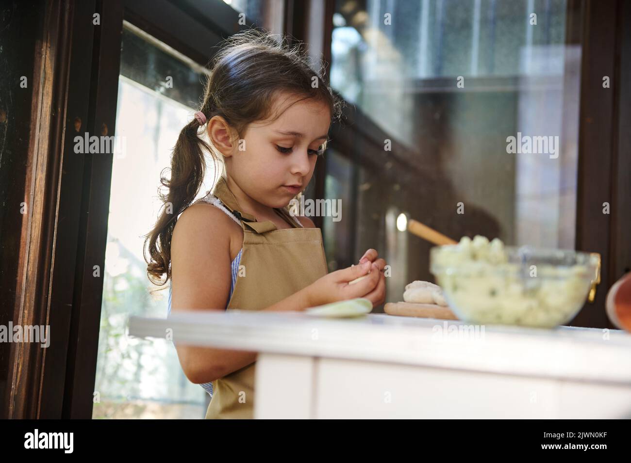 Close-up of a beautiful little cook, adorable baby girl wearing beige ...