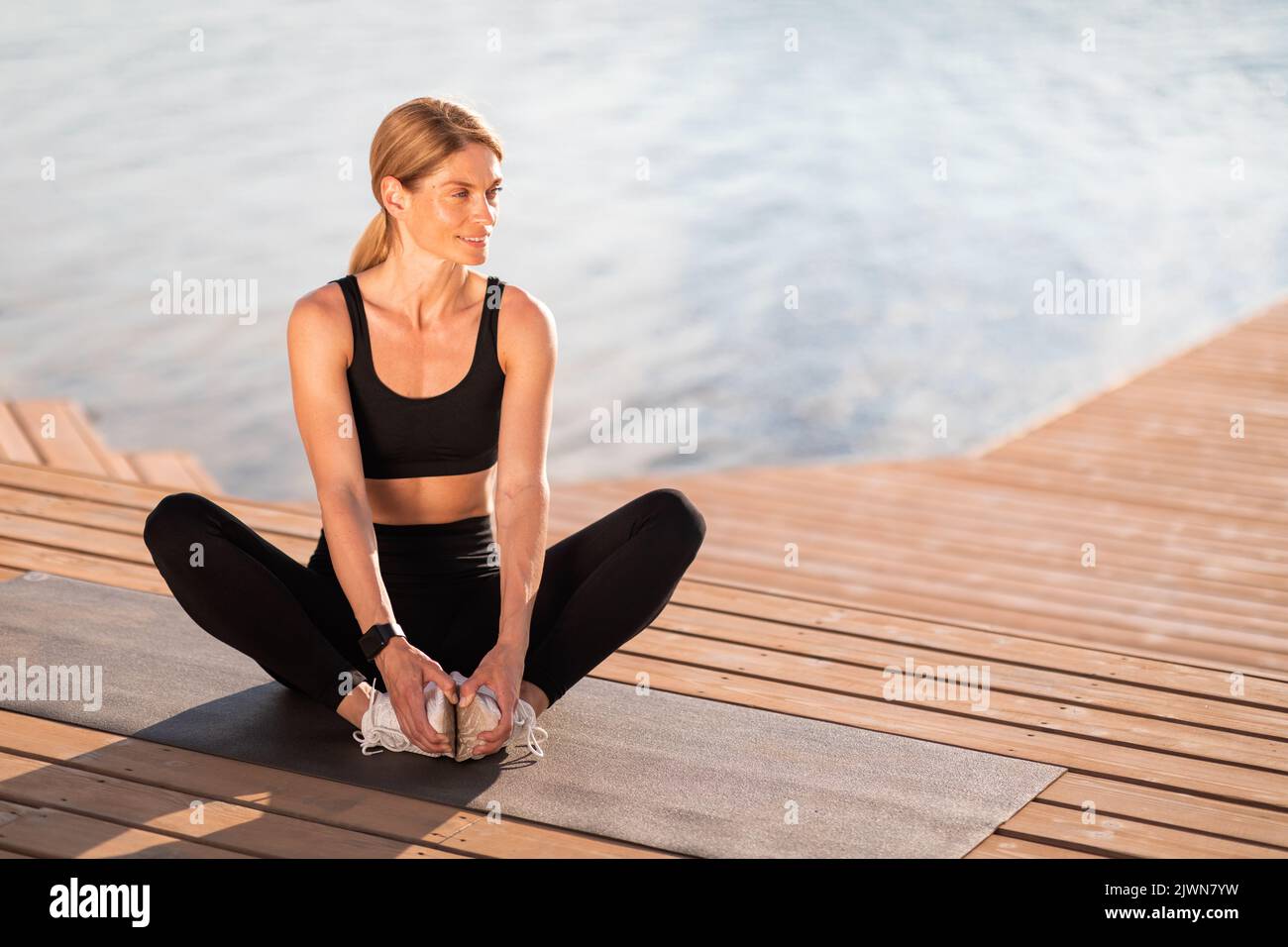 Sporty middle aged woman making butterfly stretch exercise while ...