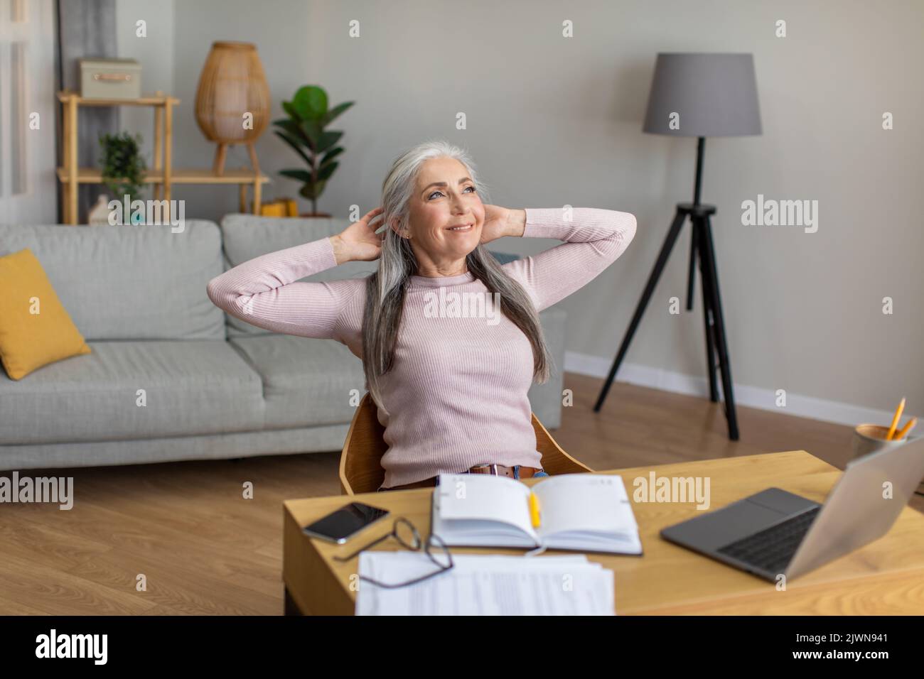 Smiling caucasian mature gray-haired lady resting from work at table ...