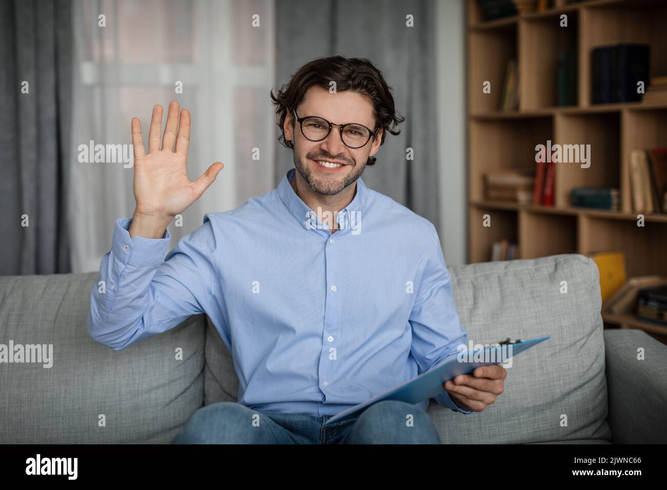 Glad cheerful young caucasian male doctor waving hand at camera in ...