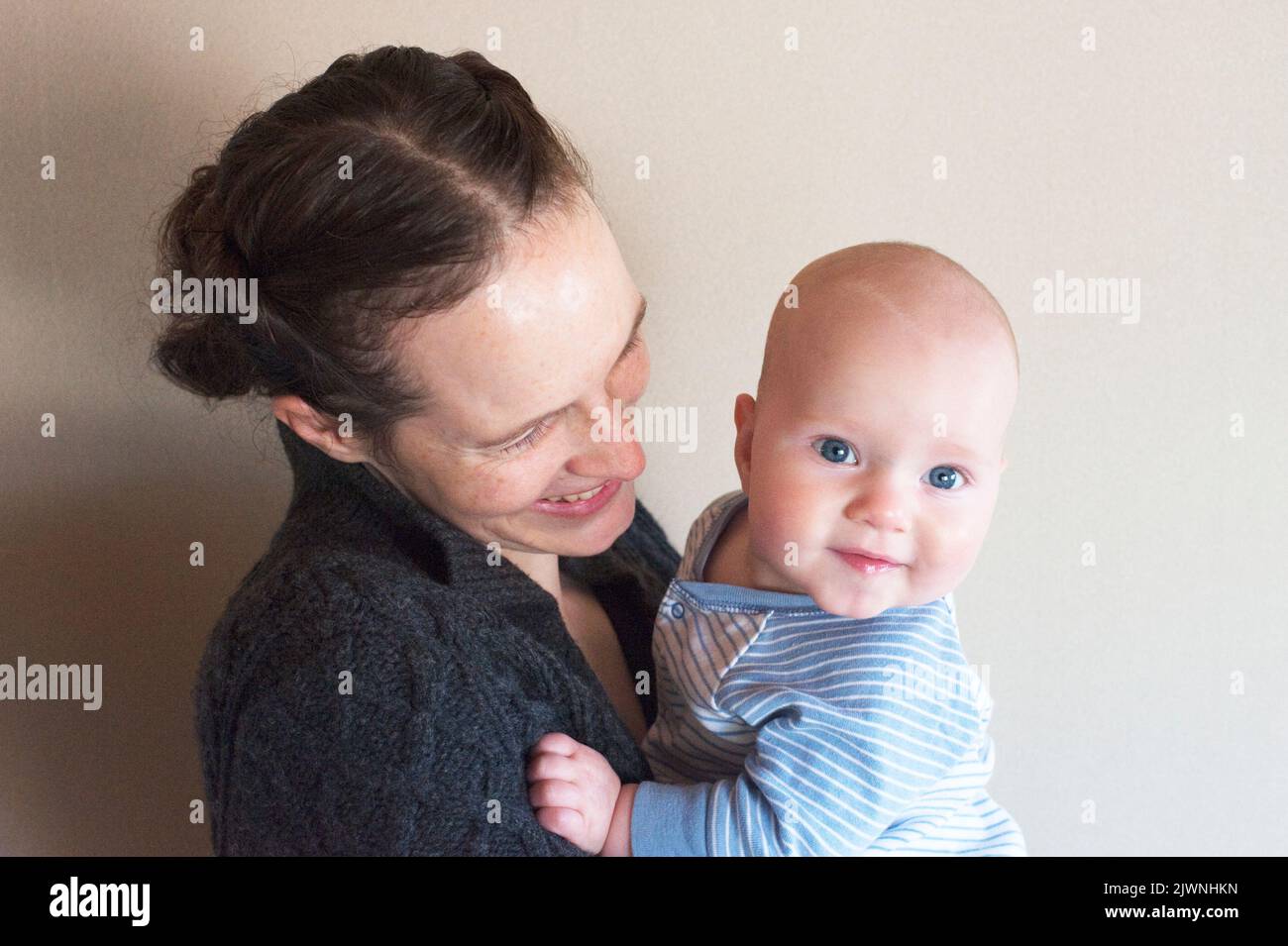 A smiling mother looks at her baby, who in turn looks at the camera ...