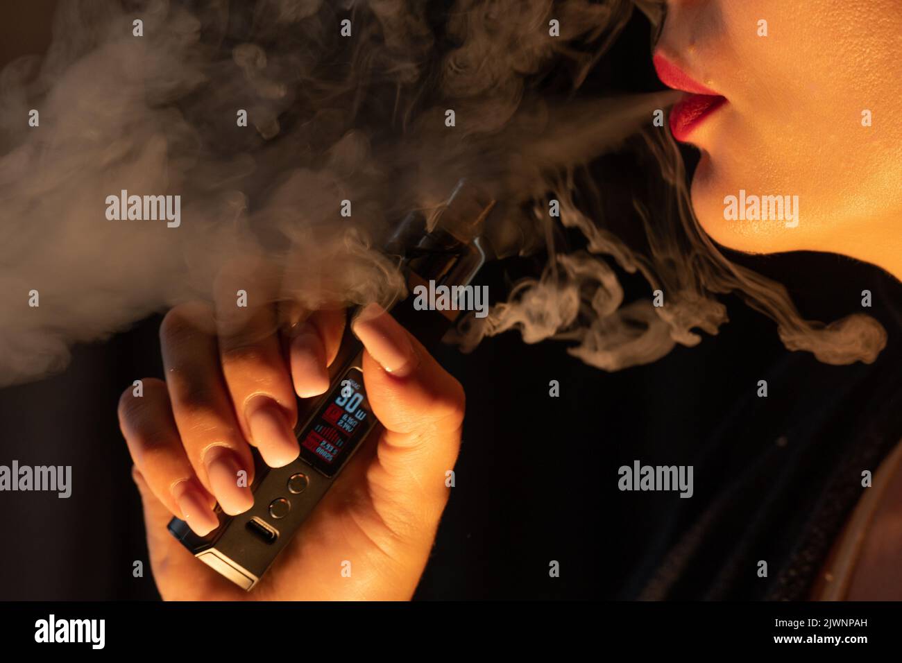 A girl smokes an electronic cigarette and exhales smoke, her lips are ...