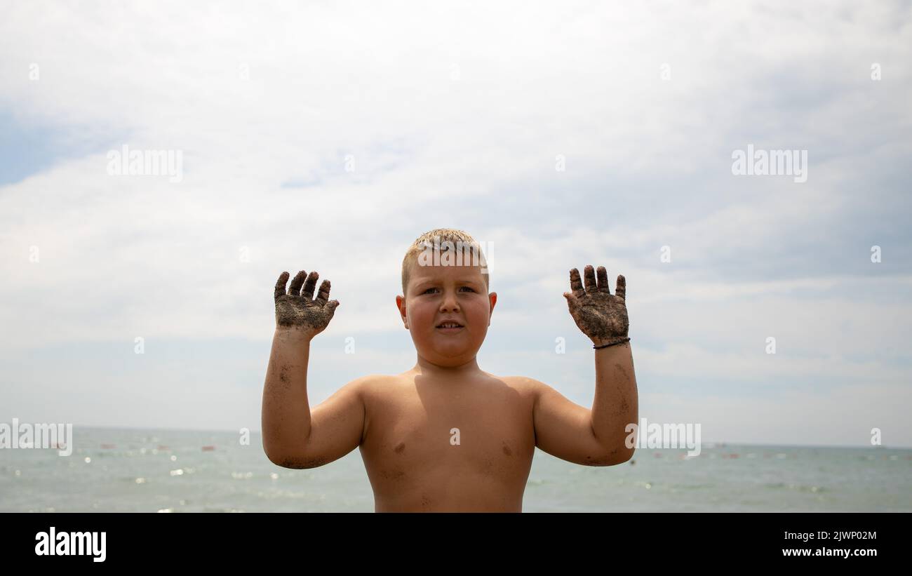 a boy on a sandy beach. the boy raised his hands and shows how the sand ...