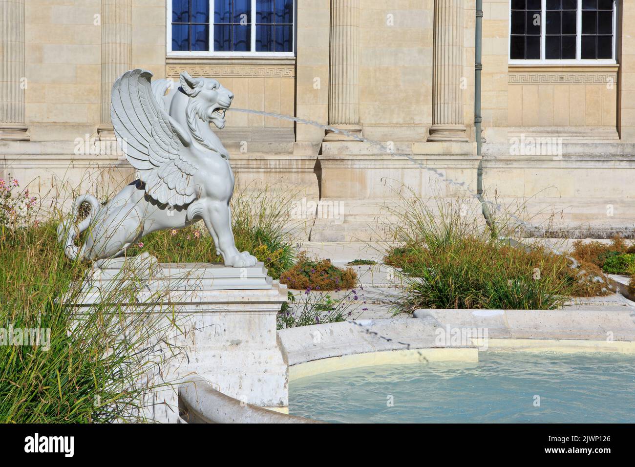 A statue of a griffin spouting water in a small pond in the gardens of ...