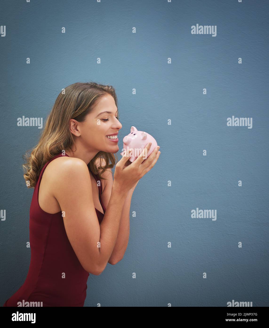 Feeling richer already. a young woman kissing a piggybank against a ...