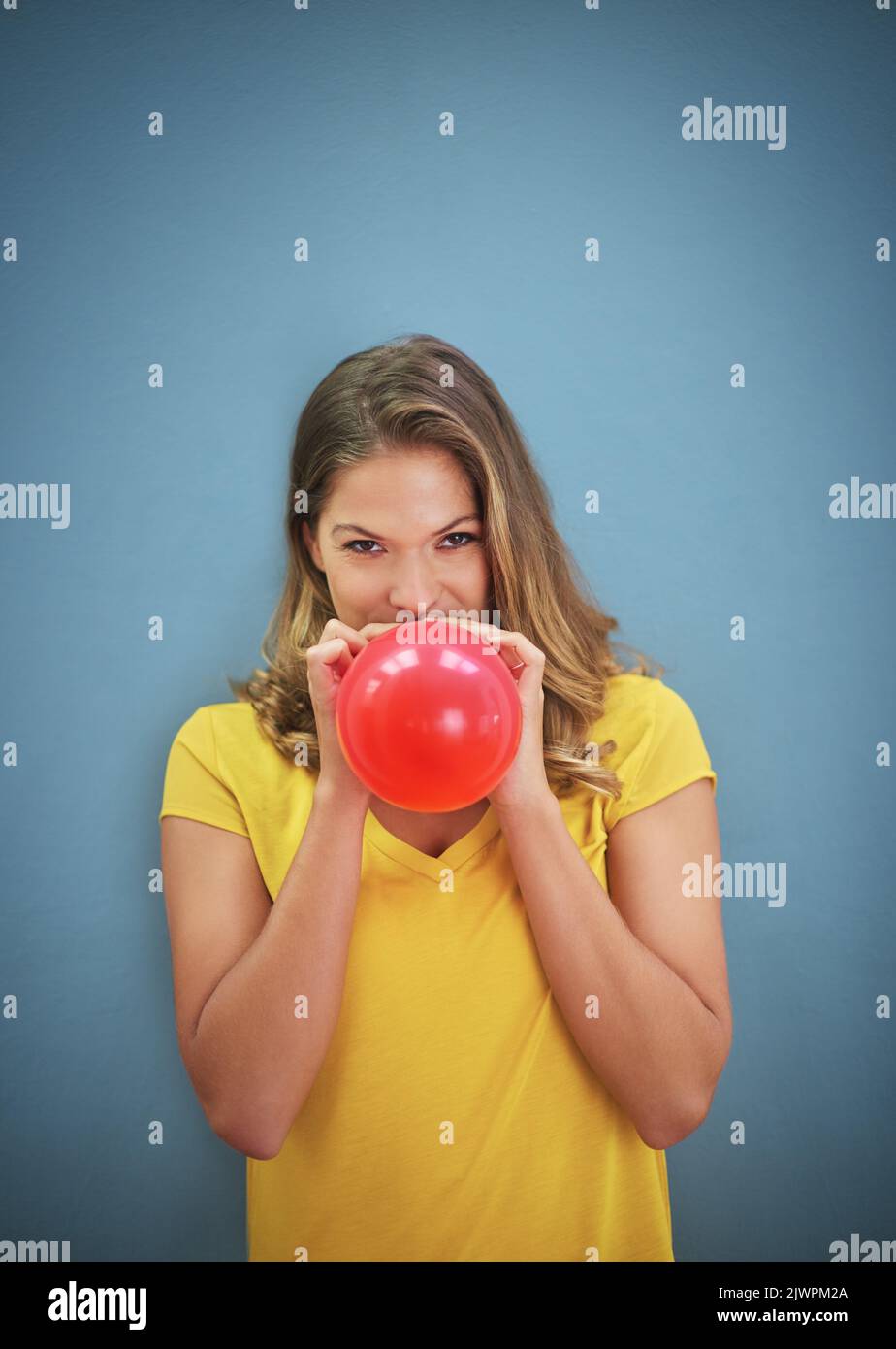Fly free. a young woman inflating a balloon against a grey background ...