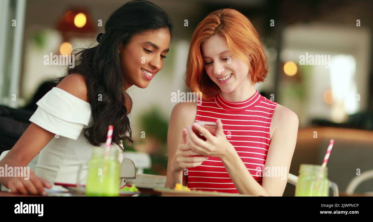 Girl showing friend cellphone screen laughing and smiling, multiracial ...