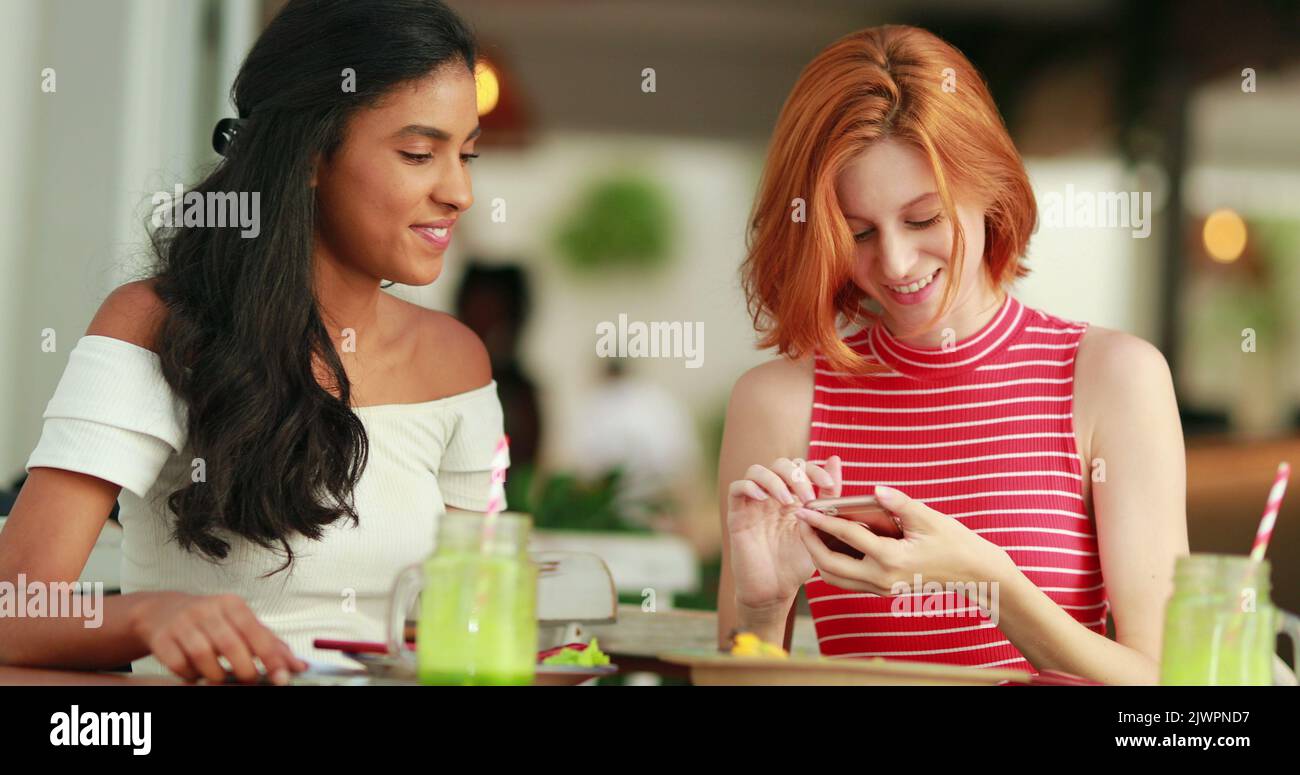 Girl showing friend cellphone screen laughing and smiling, multiracial ...