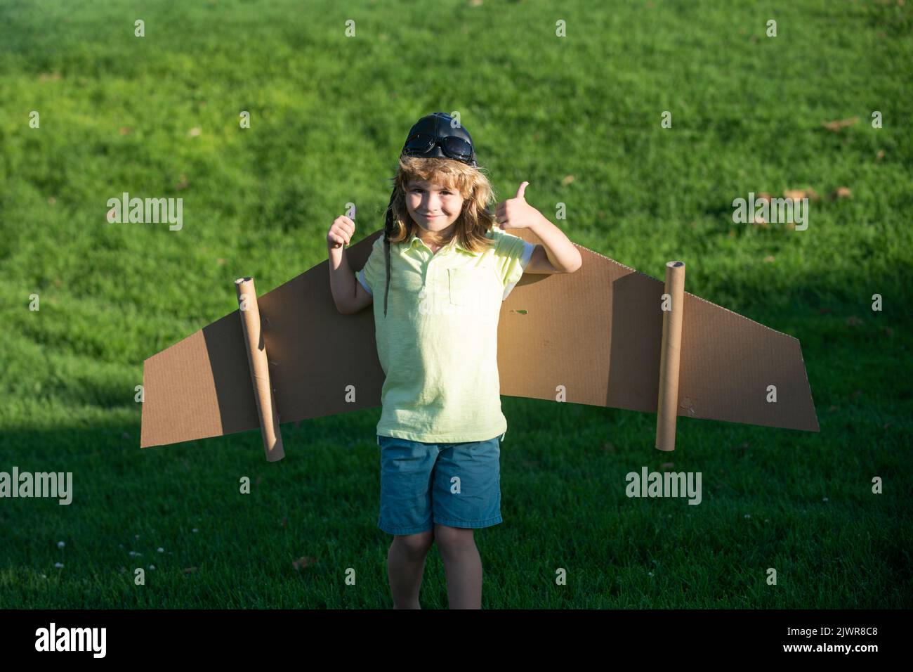 Child boy like a pilot with toy wings against green grass. Kids freedom ...