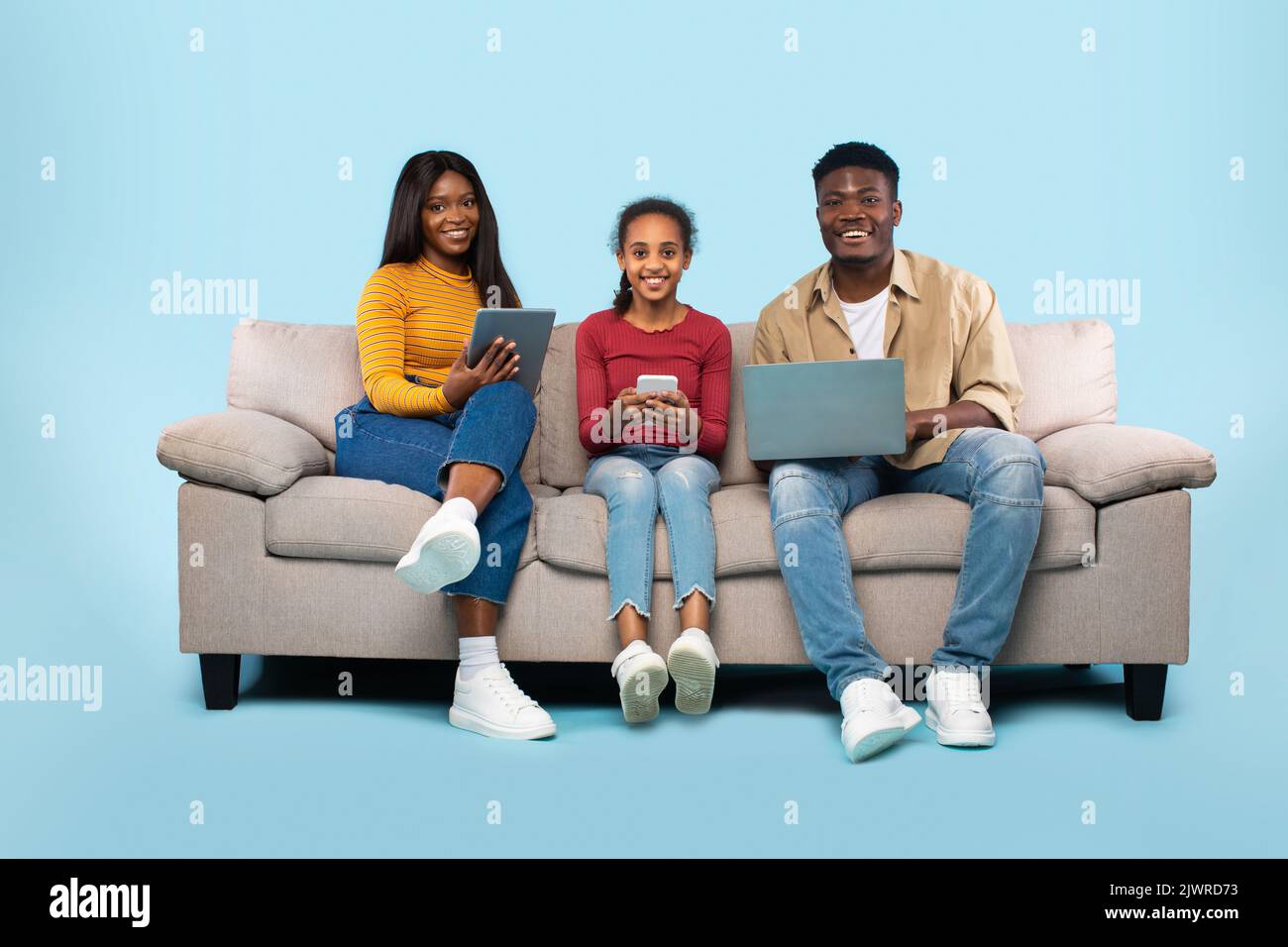 Family gadgets. Excited black parents and their daughter using ...