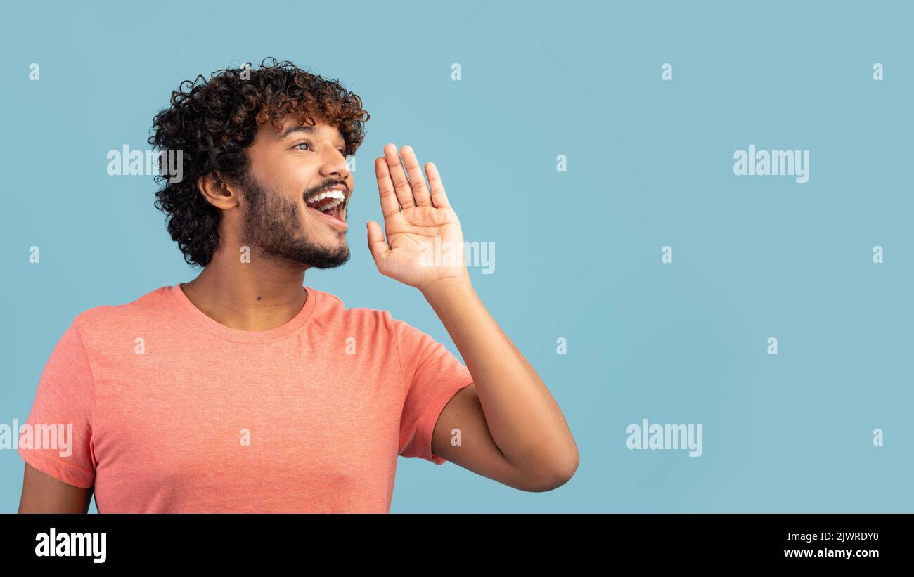 Positive hindu guy yelling towards copy space on blue Stock Photo - Alamy