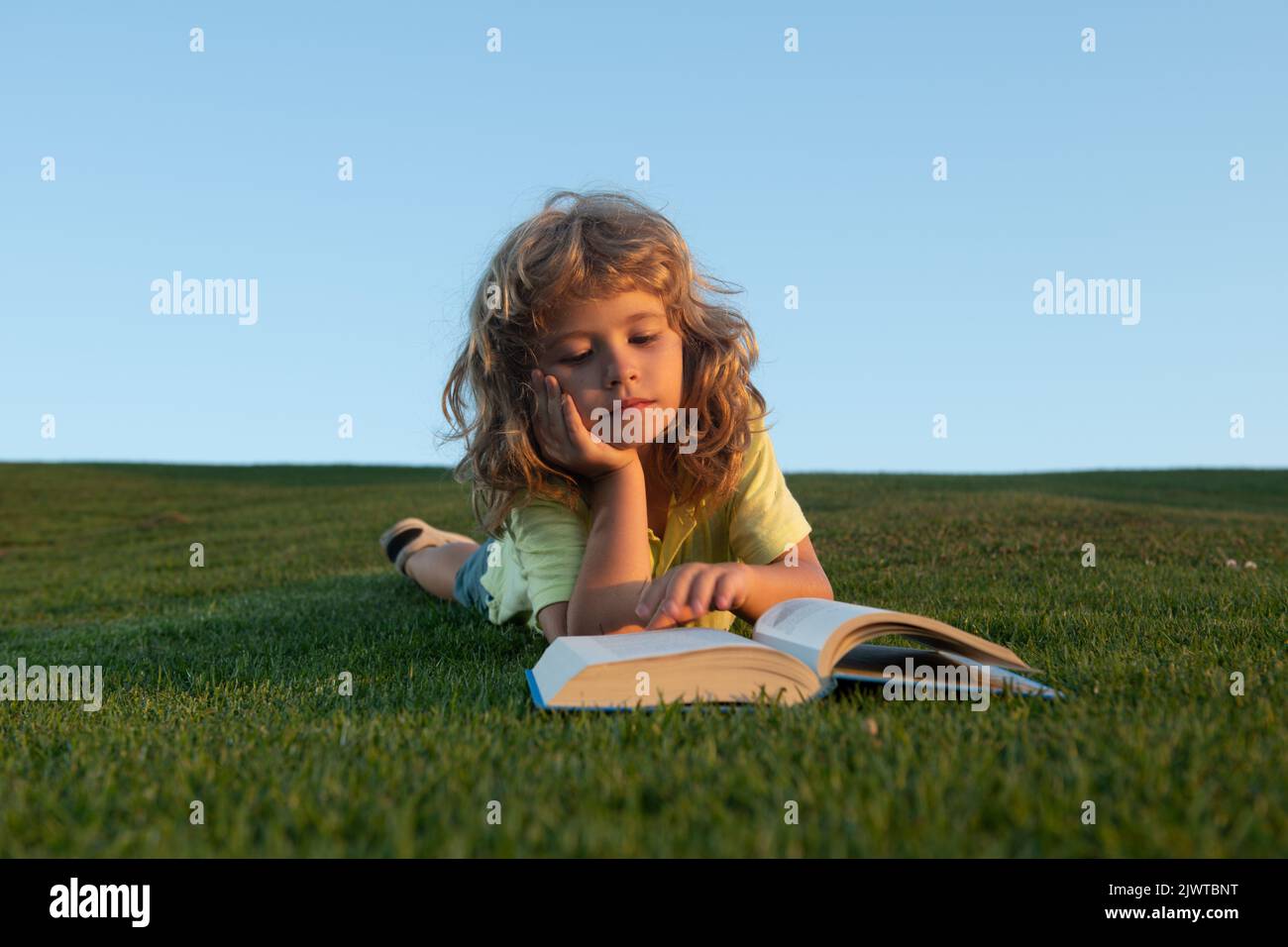 Cute kid reading book on green grass. Schoolboy with a book having a ...