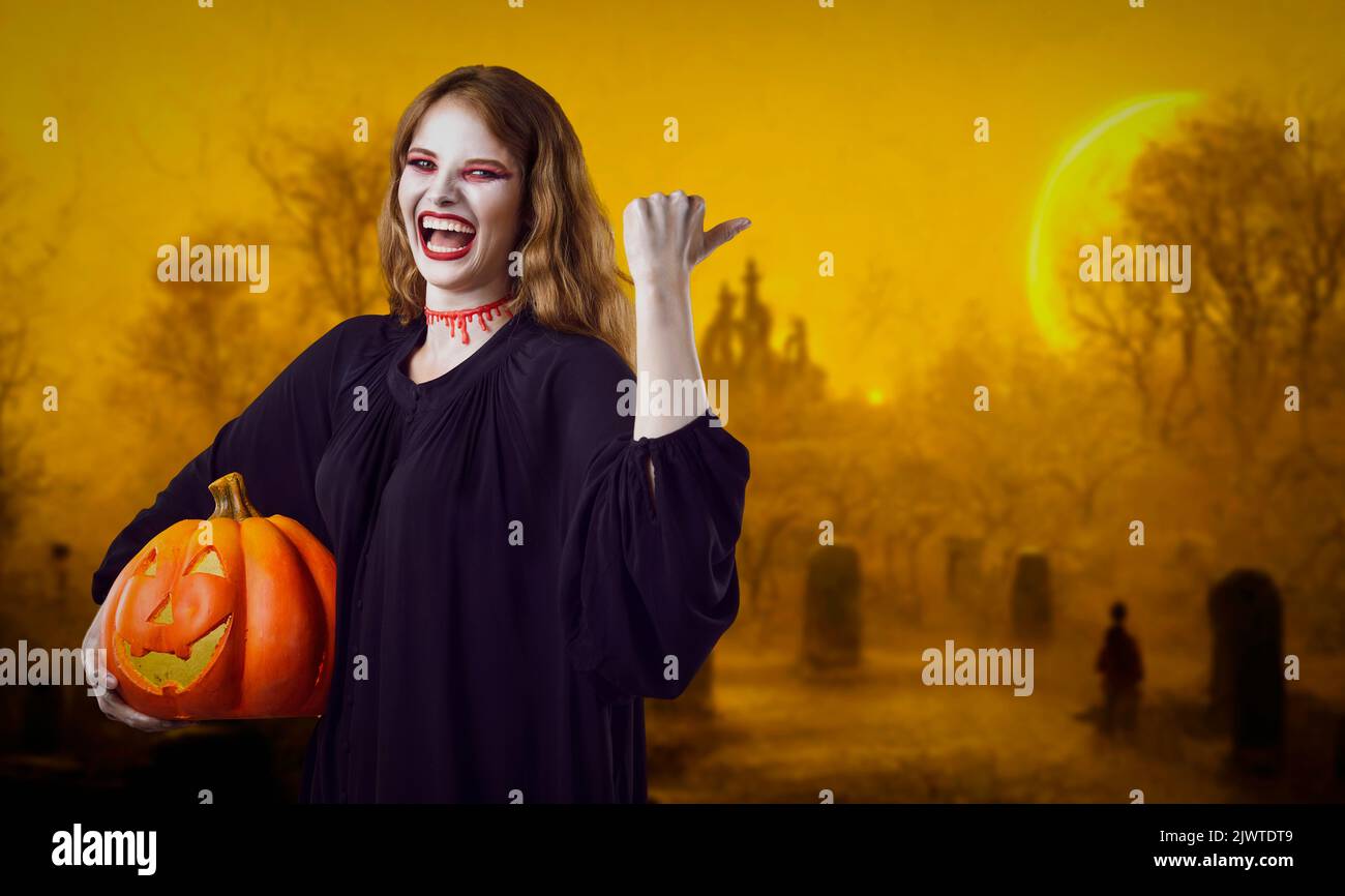Happy young woman in Halloween costume pointing at graveyard background ...