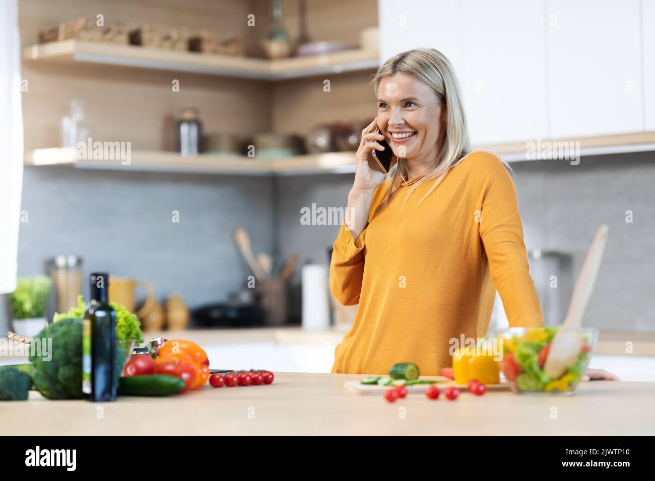 Pretty blonde woman having phone conversation while cooking Stock Photo ...