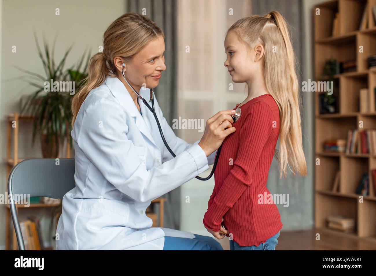 Cheerful female pediatrician listening girl's heartbeat with ...