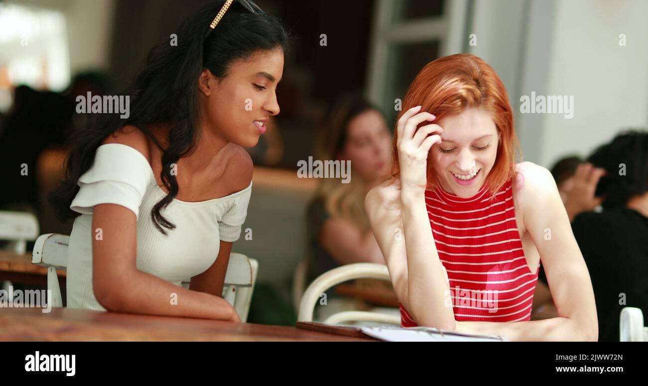 Two multiracial friends seated at restaurant talking, laughing, and ...