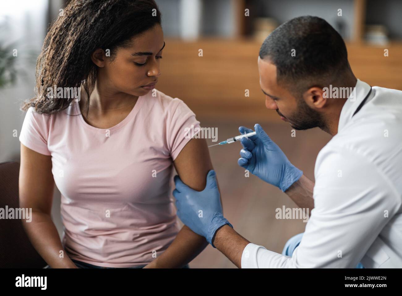 Handsome black man making injection in shoulder for female patient ...