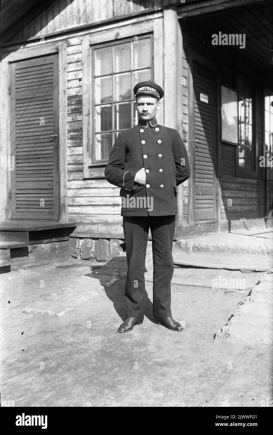 Portress poses in front of wooden building. Portvakt poserar framför ...