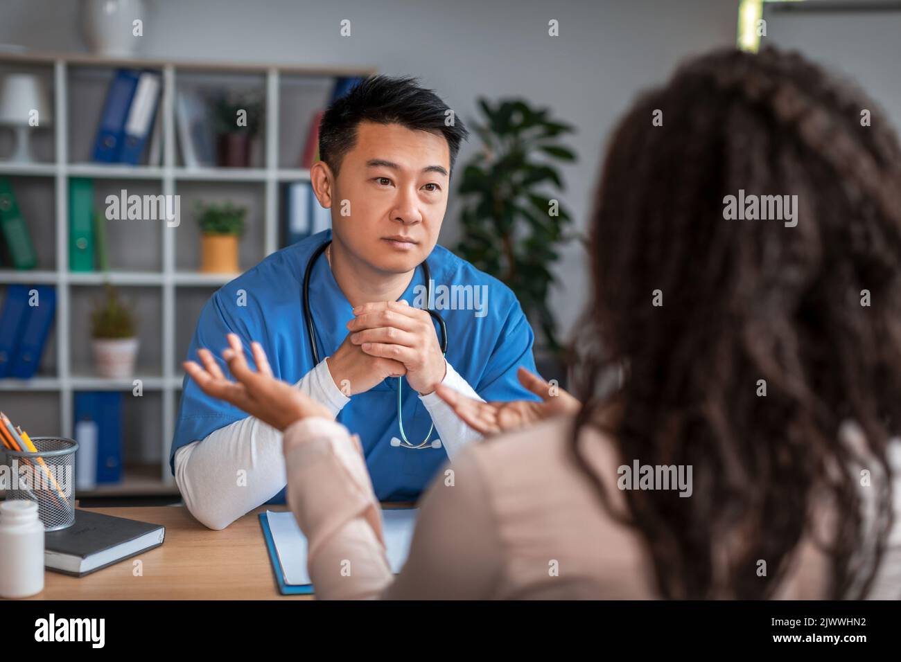 Serious millennial chinese guy doctor in uniform listens symptoms of ...
