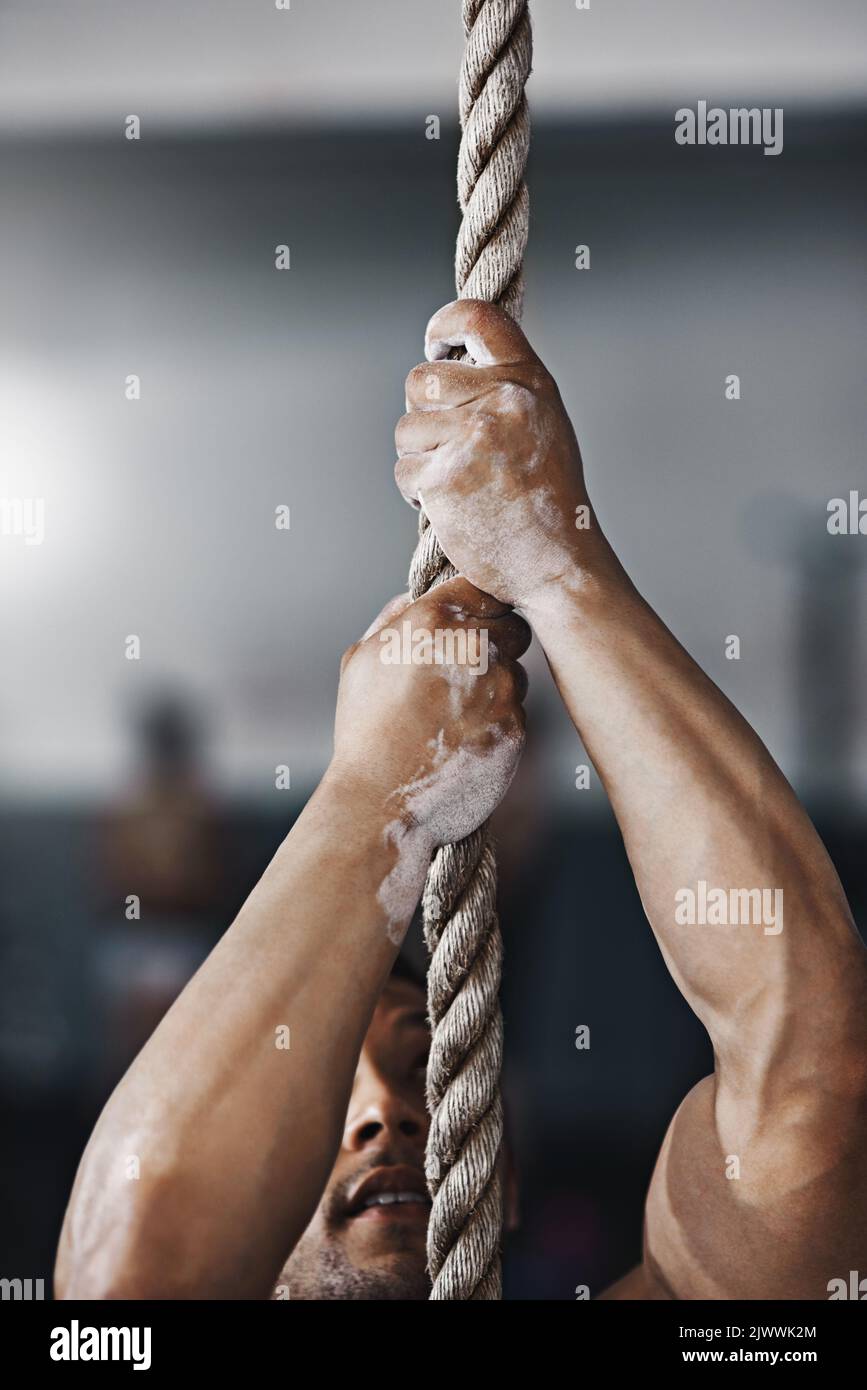 Getting a good grip. a young man climbing a rope at the gym Stock Photo ...