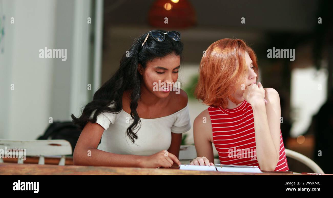 Two beautiful multiracial friends seated looking at menu and talking ...