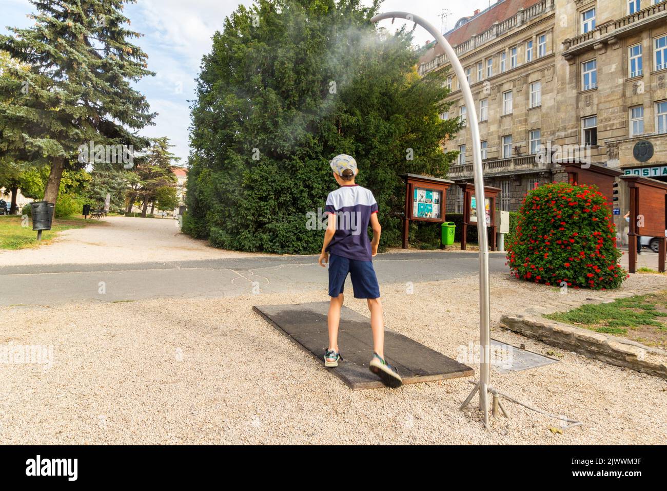 Water mist cooling system in street with boy child under during summer ...