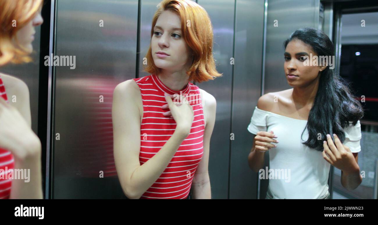 Two female friends making themselves pretty in front of elevator mirror ...