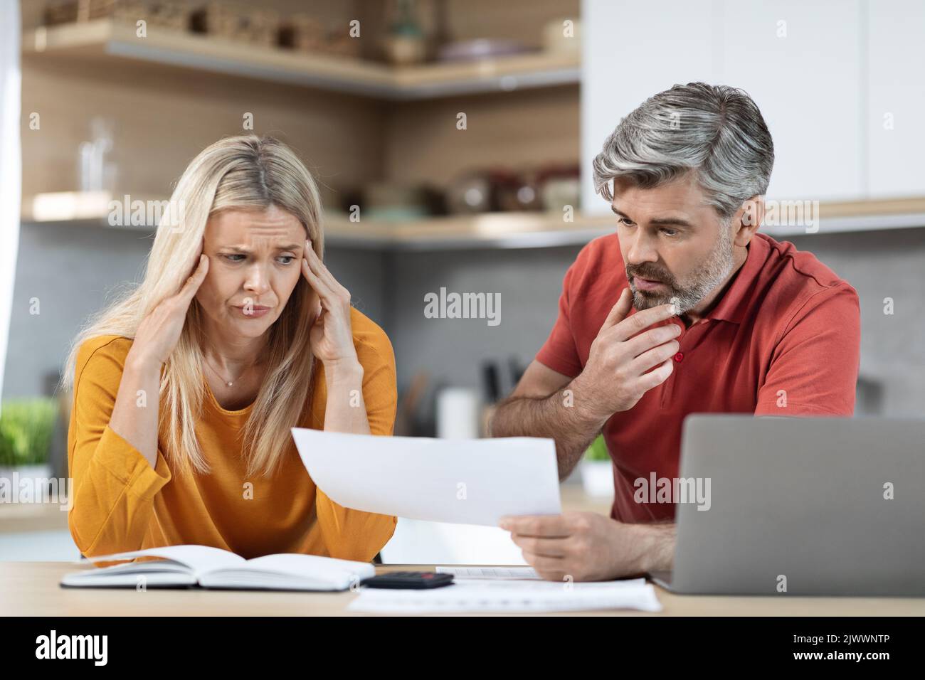Stressed husband and wife sitting at kitchen table, reading documents ...