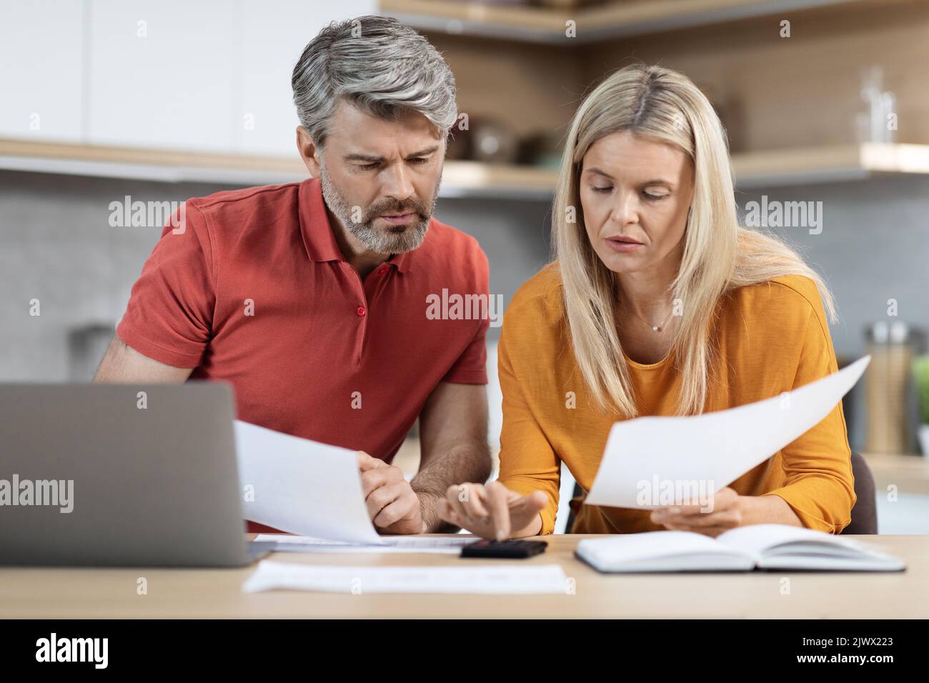 Upset middle aged husband and wife reading letter, kitchen interior ...