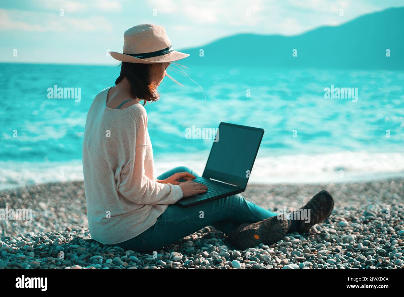 Woman sitting on a beach using a laptop computer hi-res stock ...