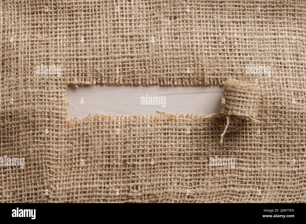 Top view of a rough linen fabric with a blank torn window in the middle ...