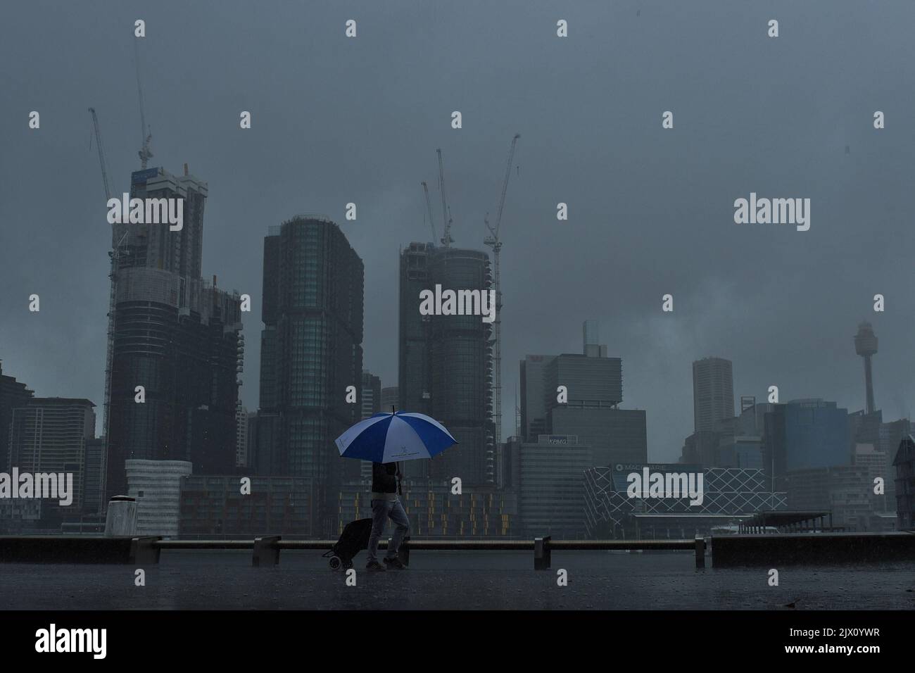 A woman walks past the Barangaroo worksite during a rain storm in ...