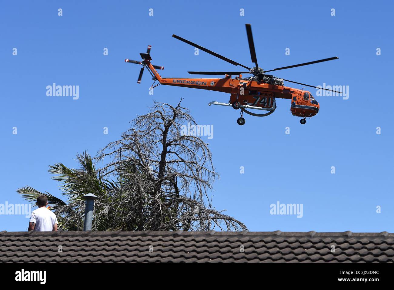 A resident watches on from his roof as an Erickson Skycrane prepares to ...