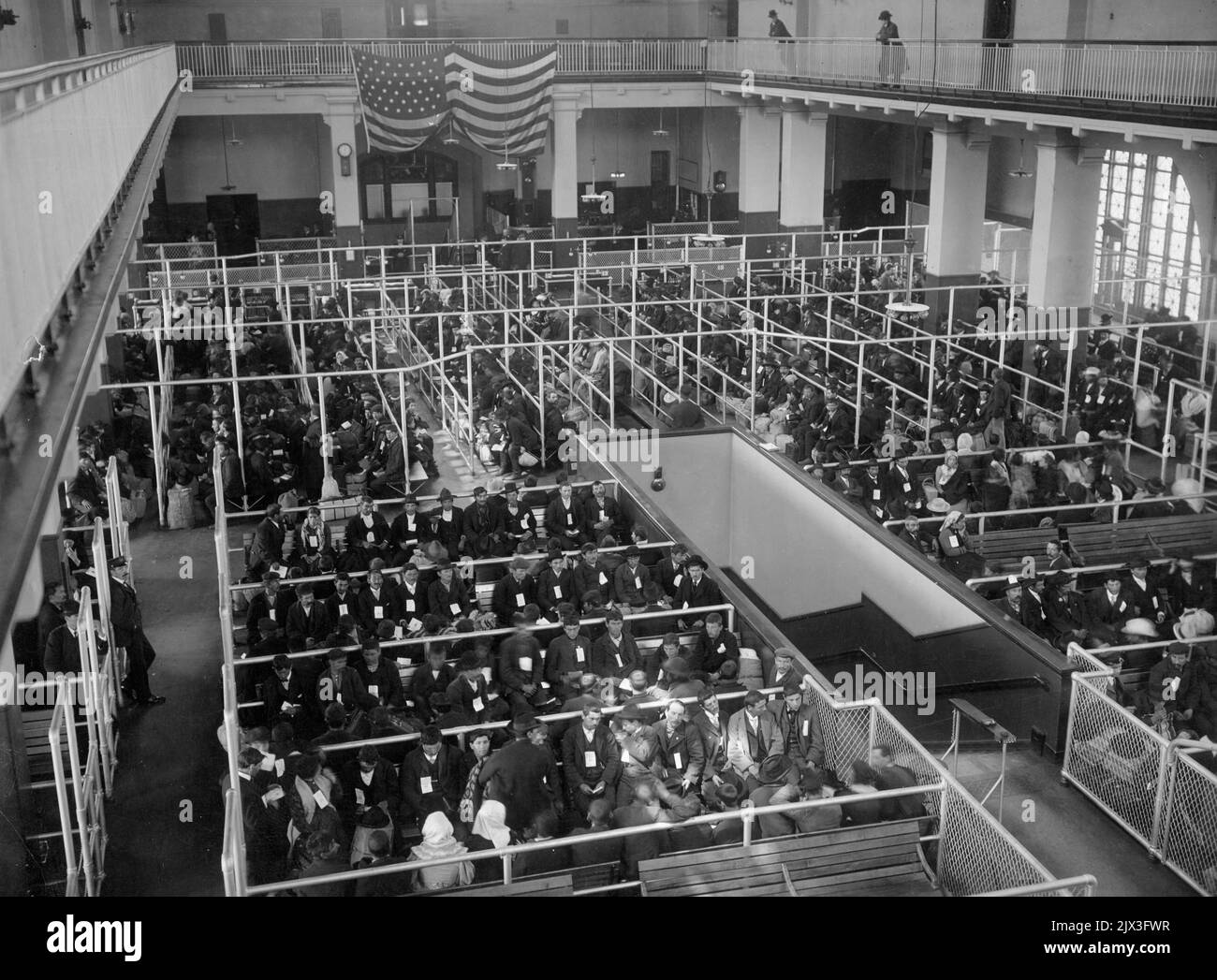Immigrants seated waiting at registry room at Ellis Island before being ...