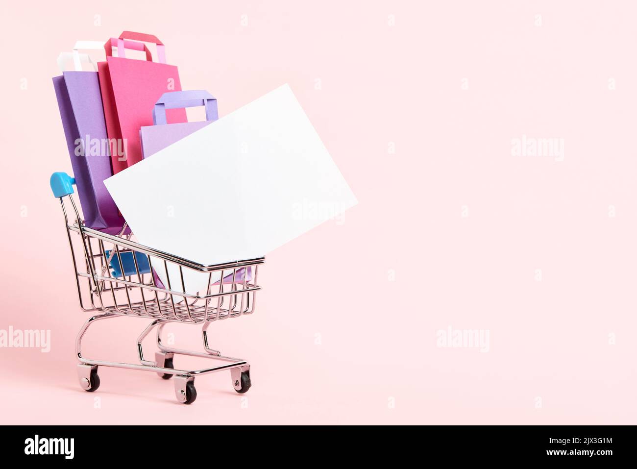 Shopping cart loaded with paper bags and a blank card on a pastel pink ...