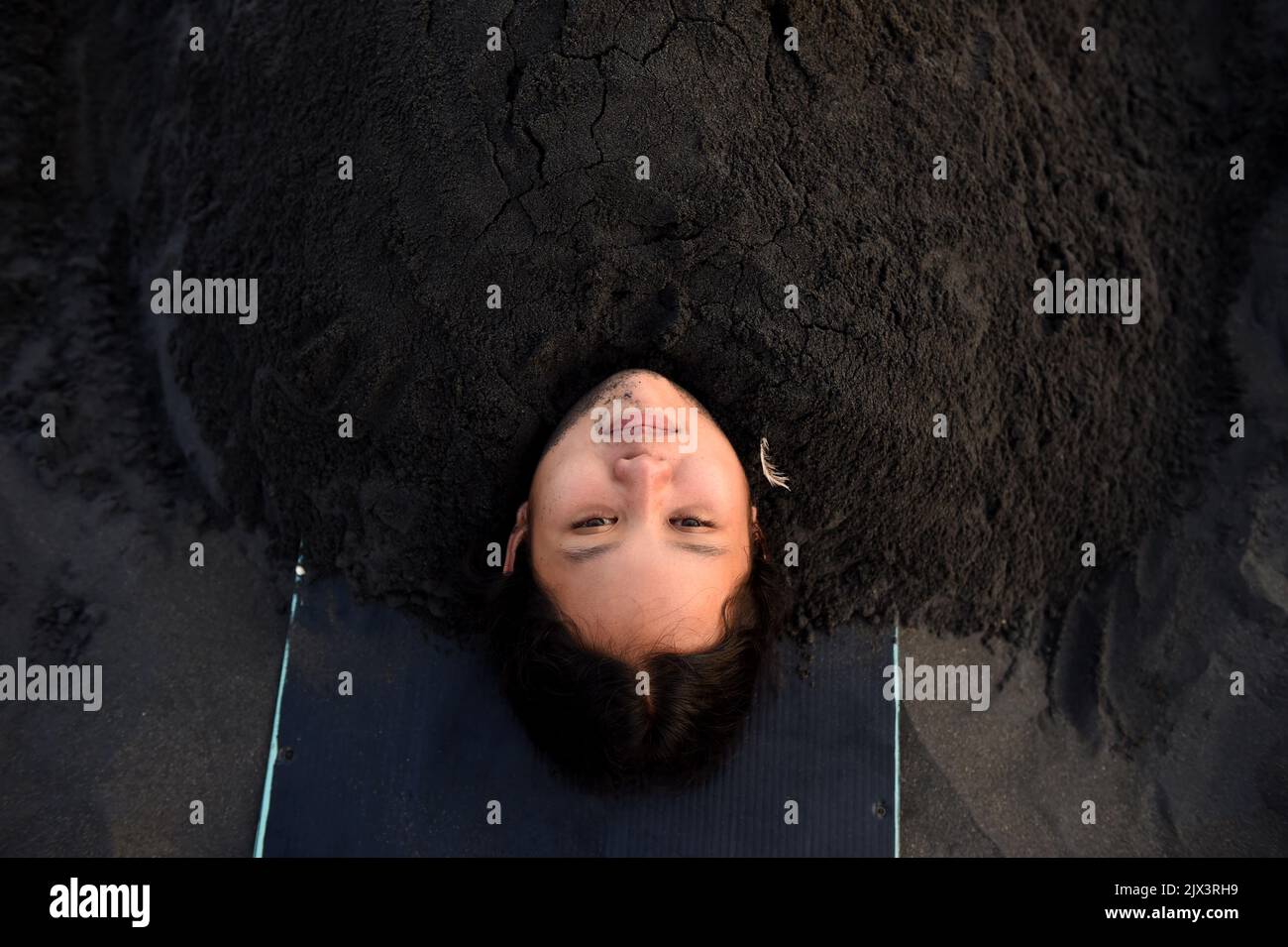 A woman is buried up to her neck in the sand on Keramas Beach, in Bali ...