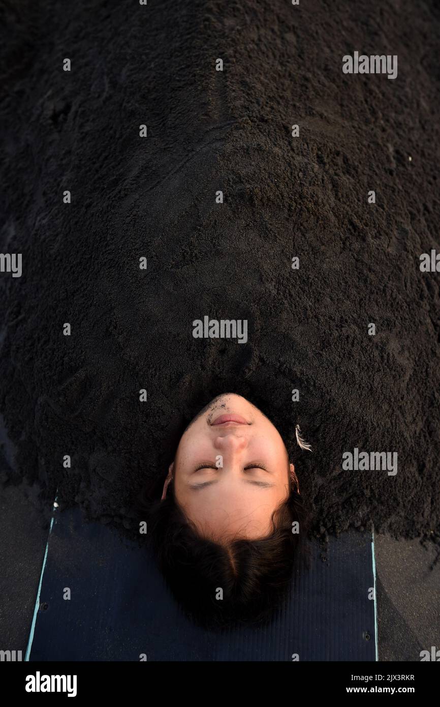 A woman is buried up to her neck in the sand on Keramas Beach, in Bali ...