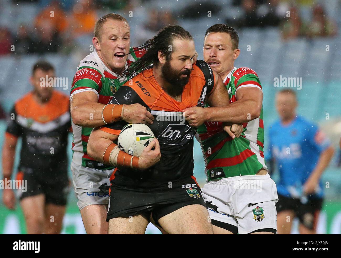 Aaron Woods of the Tigers (centre) powers his way through the Rabbitohs ...