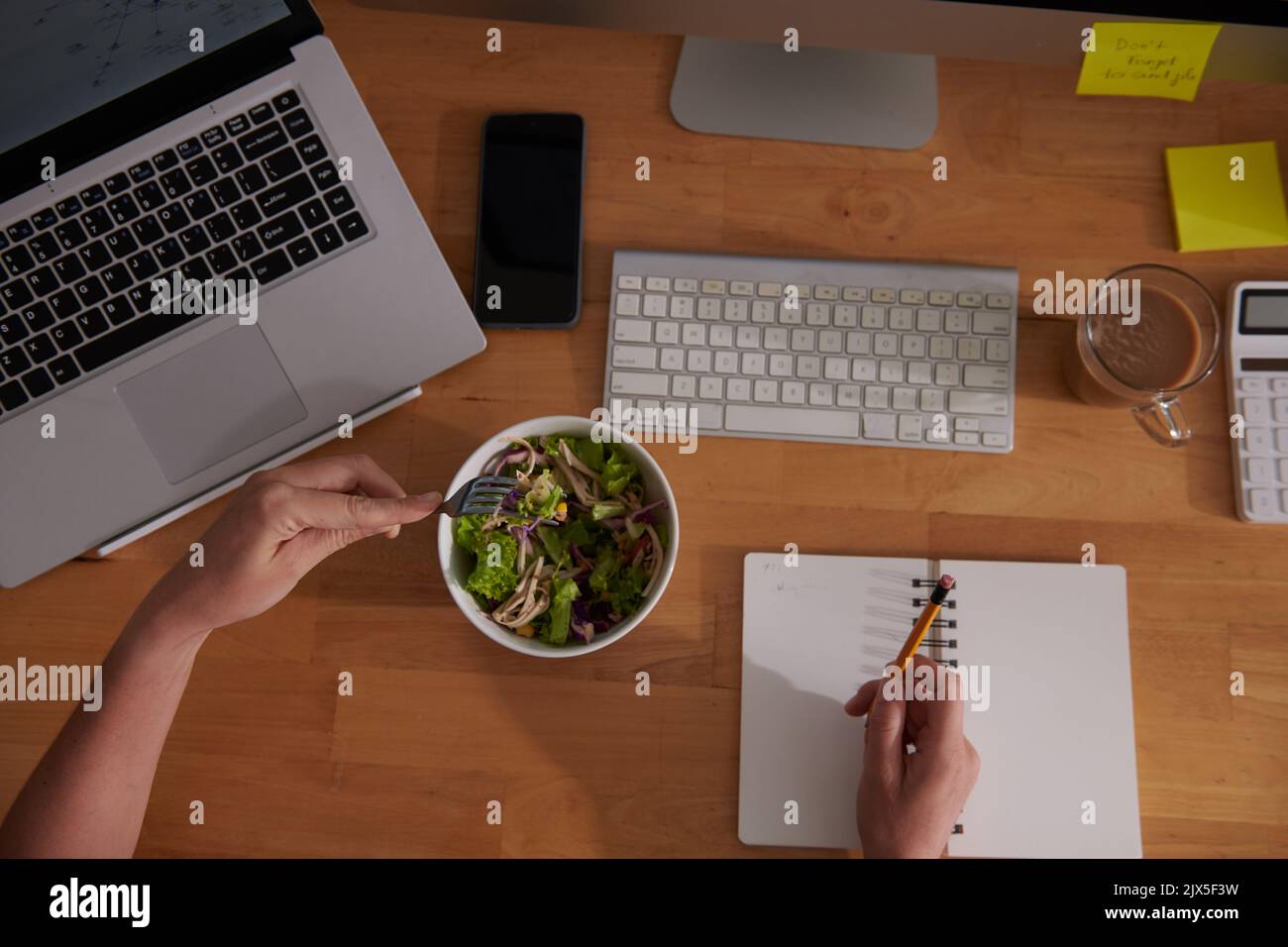 Hands of businesswoman eating healthy salad and writing in planner ...