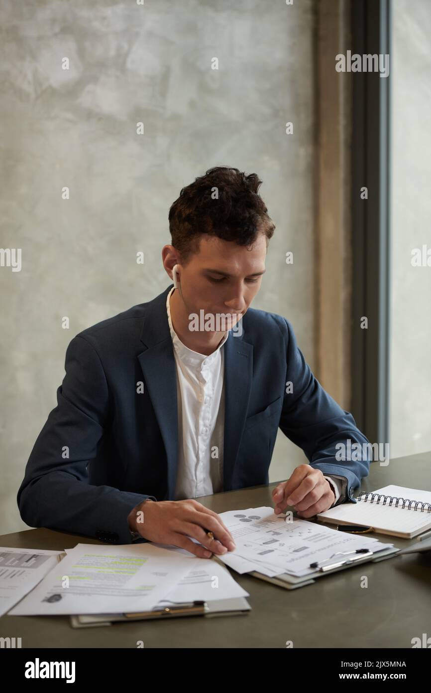 Pensive entrepreneur checking reports and documents on table in front ...