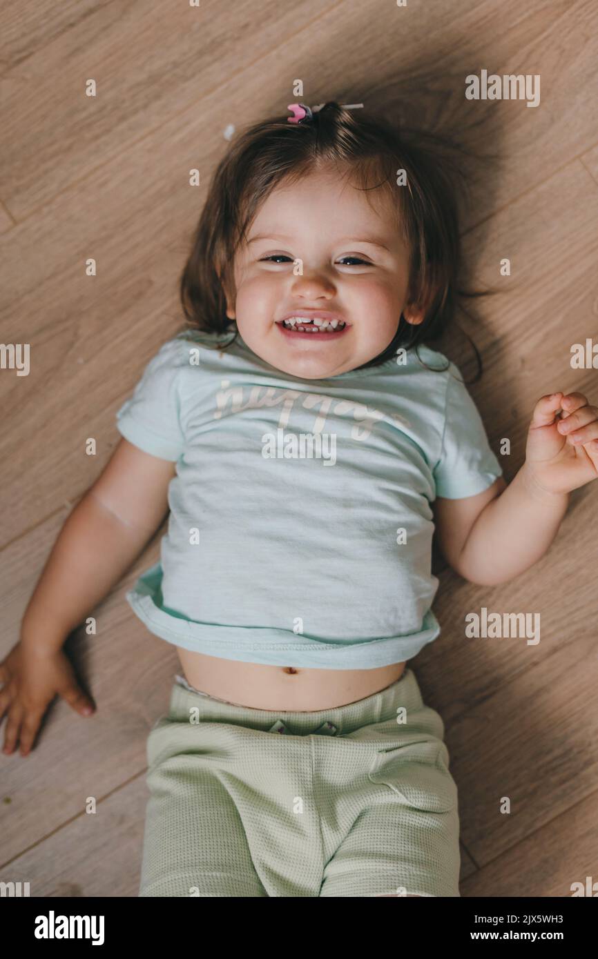 Happy little baby girl smiling at camera while lying on her bed on the floor. Top view. Beauty ...